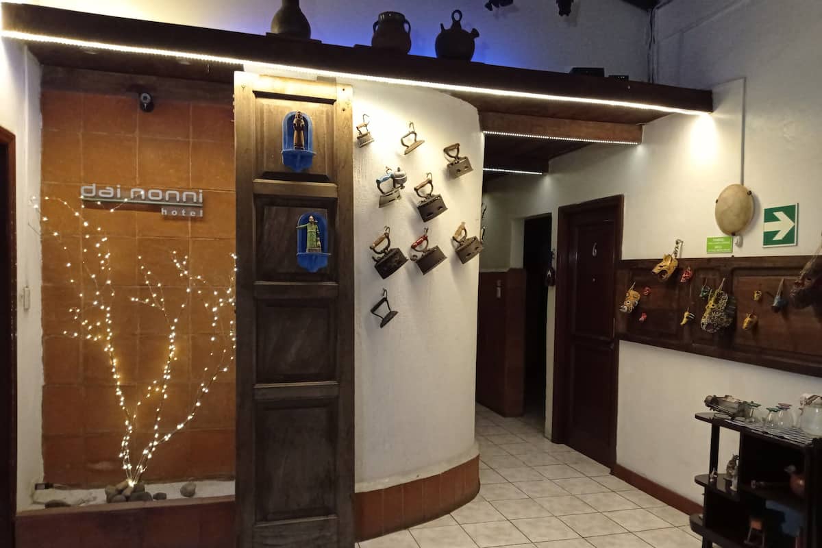 Um hall de hotel com uma mesa de recepção de madeira, um porta-casacos fixado na parede com várias bolsas e uma placa indicando o nome do hotel.