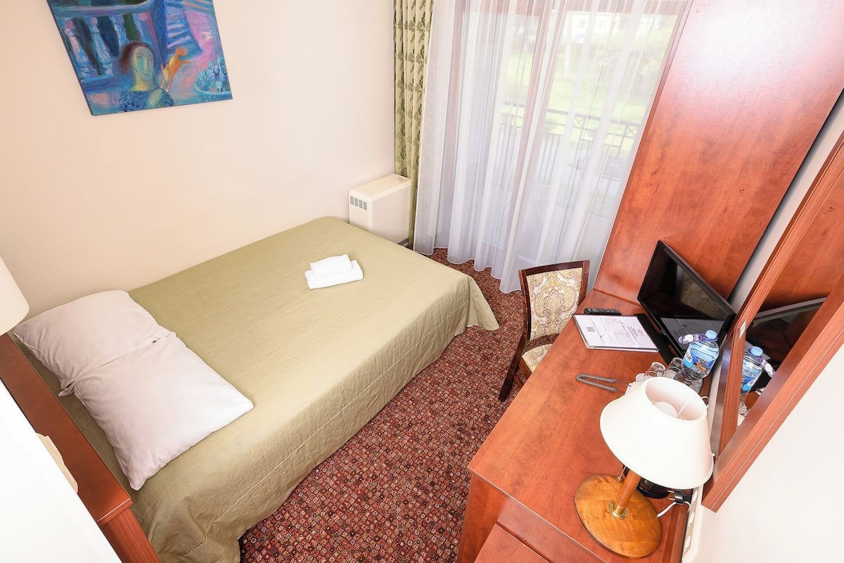 Quarto de hotel com uma cama, uma mesa com um computador, uma luminária e um quadro na parede.