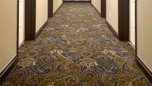 Corredor de hotel com carpete estampado, portas e uma pintura grande na parede.