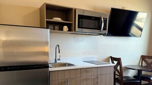 Uma cozinha compacta com geladeira, micro-ondas, pia e uma TV de tela plana instalada acima do micro-ondas.