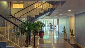 Um hall amplo com escadaria moderna, plantas em vasos e piso lustroso.
