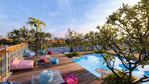 Área de piscina no terraço com deck de madeira, espreguiçadeiras e almofadas coloridas.