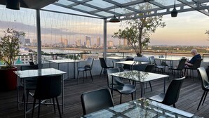 Terraço no telhado com mesas e cadeiras de vidro, com vista para a paisagem urbana e rio.
