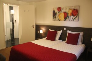 Quarto de hotel com uma cama grande, um quadro de tulipas na parede, chuveiro e mesa de cabeceira com abajur.