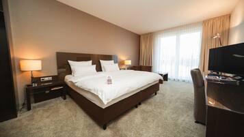 Quarto de hotel com uma cama grande, duas mesas de cabeceira com abajures, uma escrivaninha com uma TV e vista para a cidade pela janela.