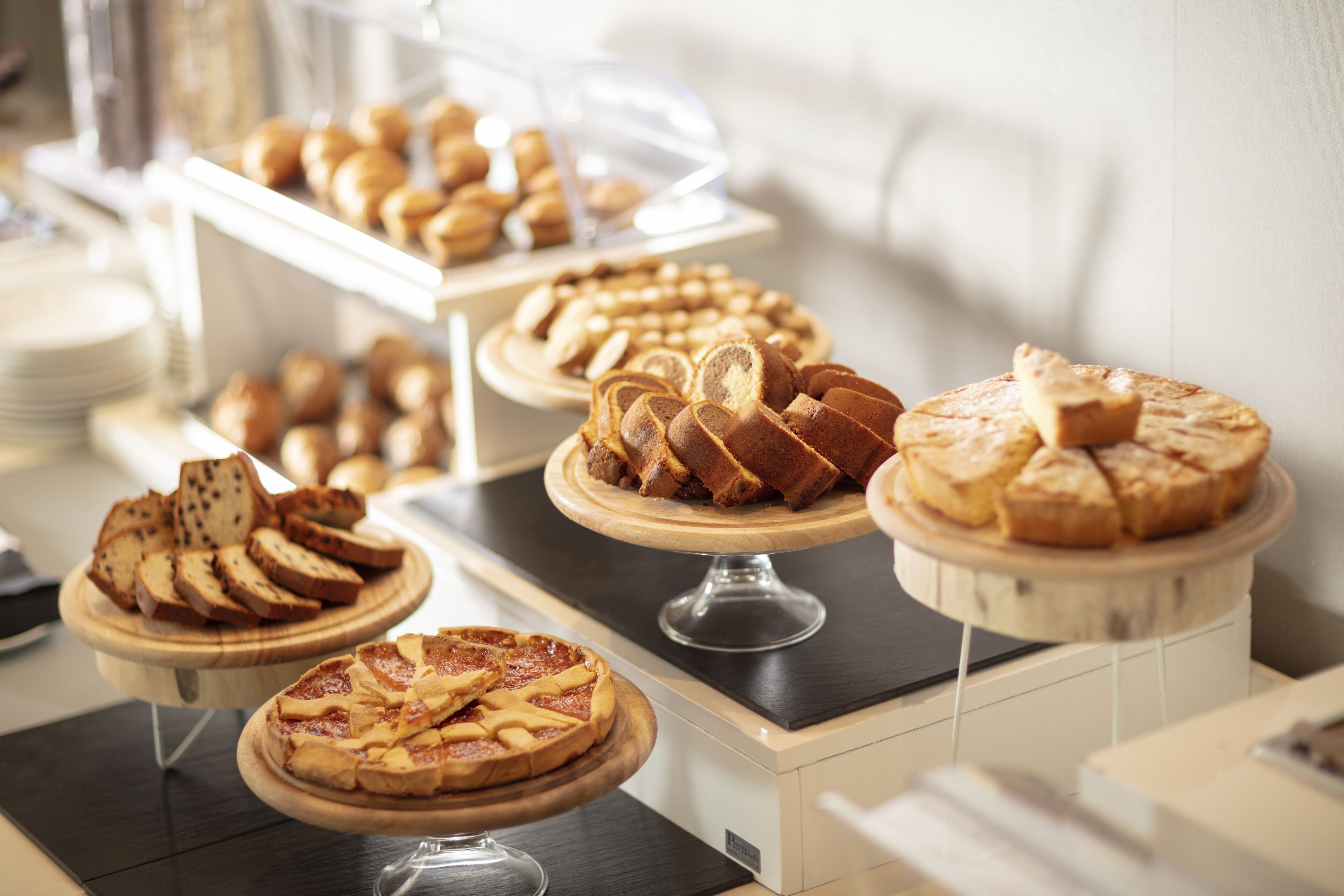 Buffet com diversos produtos de panificação, incluindo pão, tortas e doces, expostos em suportes de madeira.