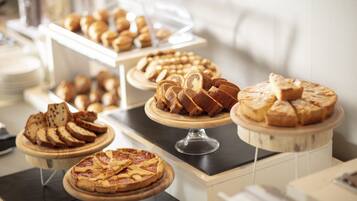 Buffet com diversos produtos de panificação, incluindo pão, tortas e doces, expostos em suportes de madeira.