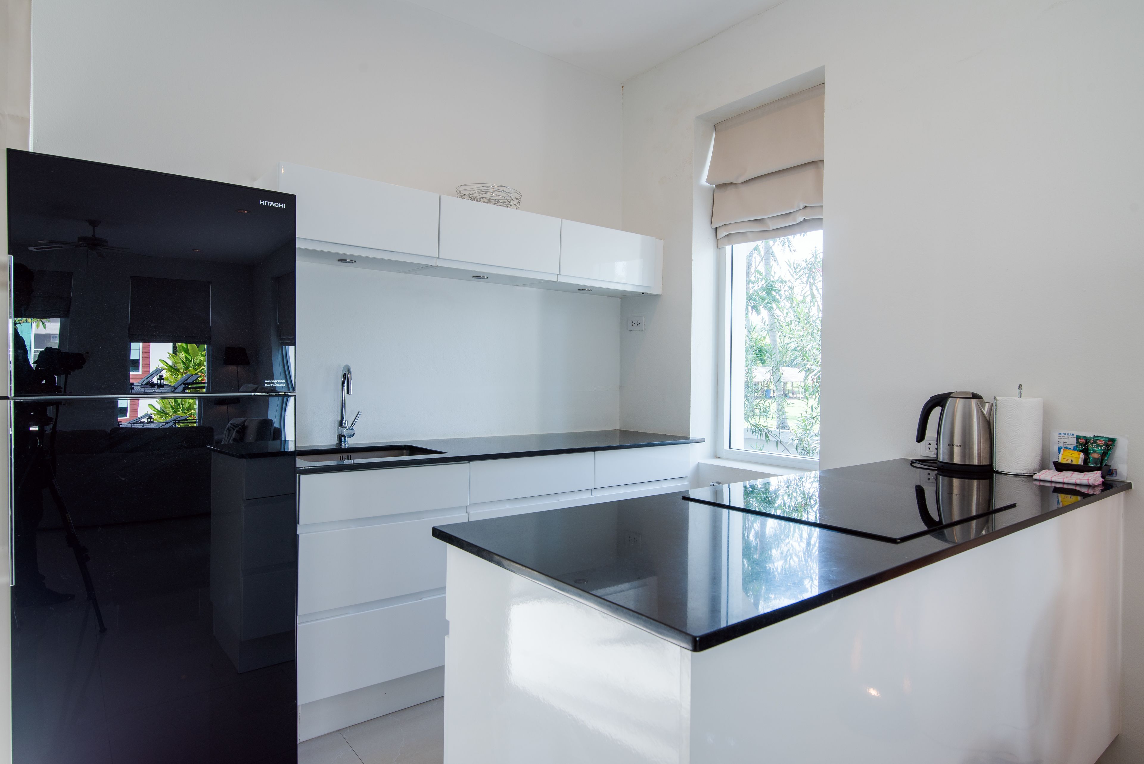Uma cozinha moderna com armários brancos, bancada preta e janela com cortinas bege.