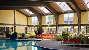 Uma área de piscina com barreira de vidro, cadeiras de espreguiçadeira e um espaço de estar coberto com vista para o exterior.