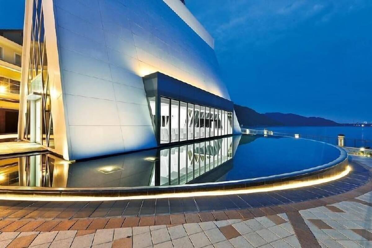 Um edifício moderno com piscina refletora e fachada de vidro curva.
