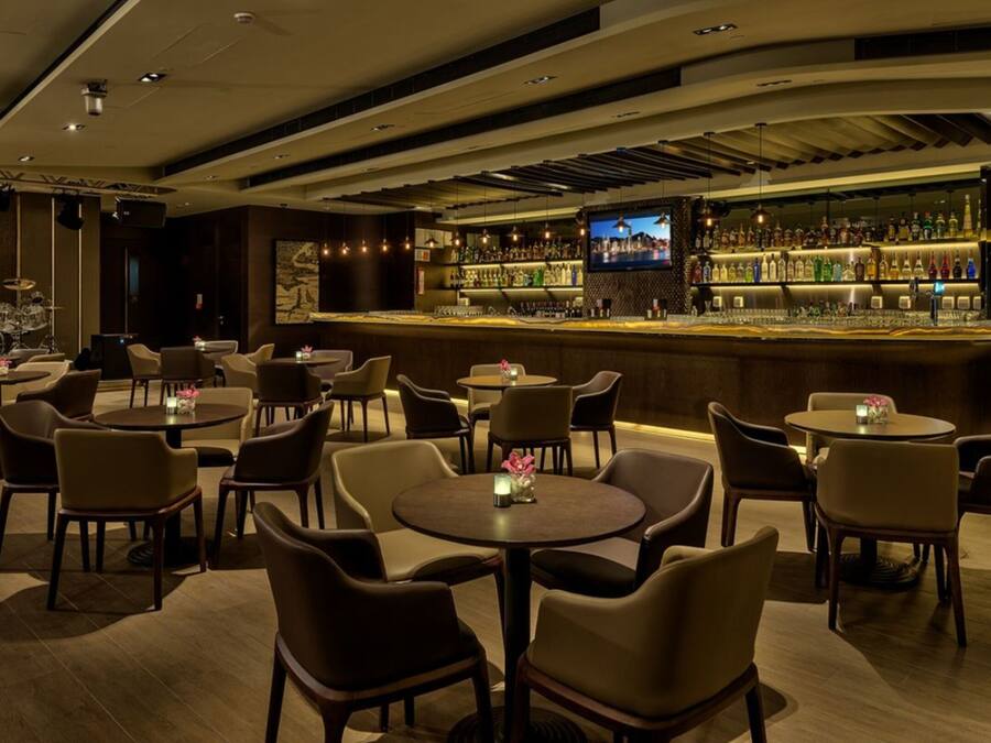 Uma área de bar com diversas opções de assento, palco com instrumentos musicais e um balcão de bar bem abastecido.
