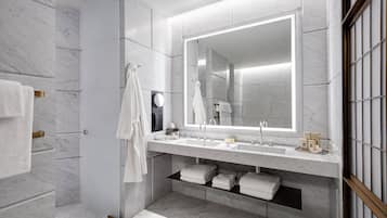 Um banheiro moderno com um espelho grande, azulejos de mármore branco, chuveiro embutido e toucador com pia e espaço para toalhas.