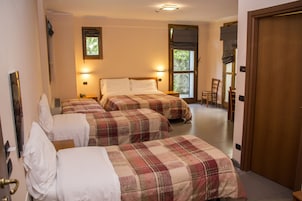 Quarto de hotel com duas camas, uma porta de madeira e uma janela com vista para árvores.