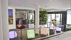Um hall de hotel moderno com guarda-corrimão de vidro, áreas de estar e uma grande parede verde com plantas.
