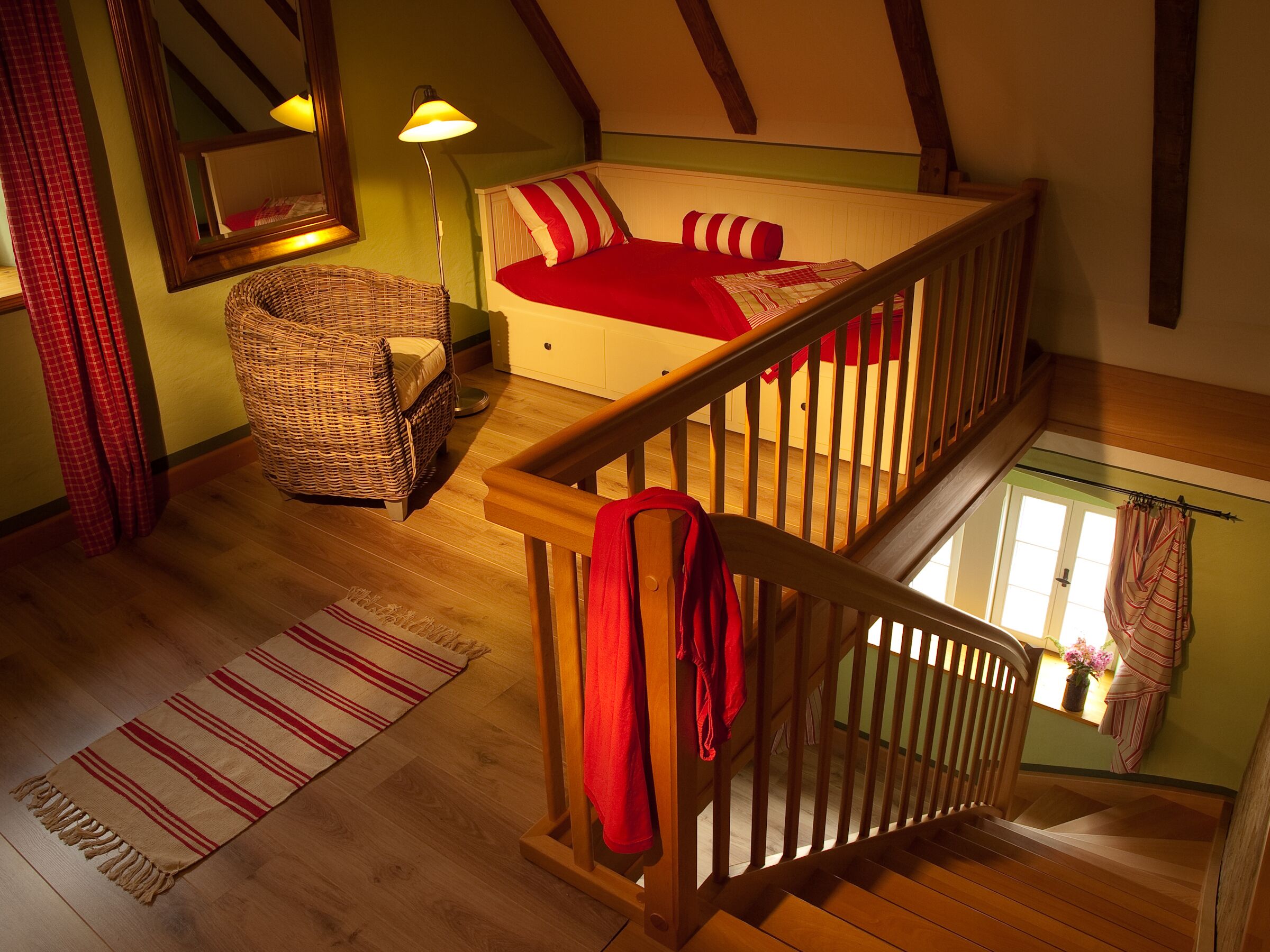 Quarto aconchegante com escada de madeira, uma cadeira de vime e cama com roupa de cama listrada.