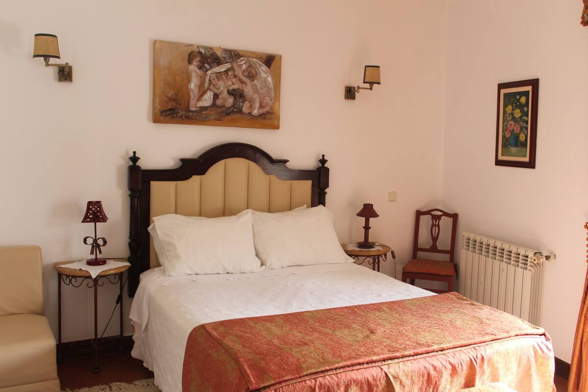 Quarto com cama, duas mesas de cabeceira, uma cadeira e um radiador.
