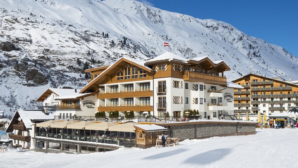Um hotel grande com vários andares e varandas, cercado por montanhas cobertas de neve.