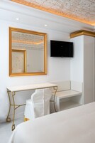 Quarto de hotel moderno com um espelho grande, televisão de tela plana, escrivaninha branca e uma cama.