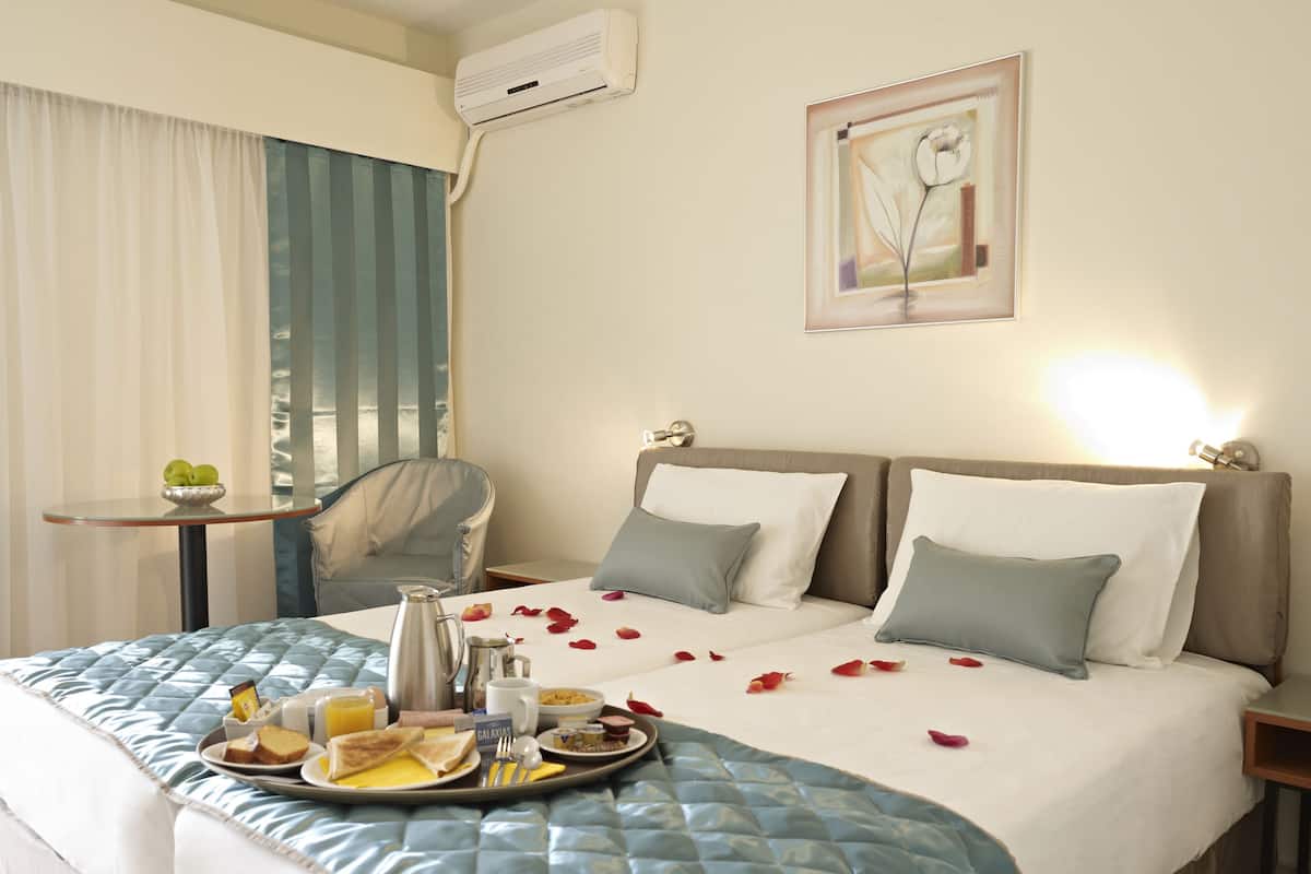 Quarto de hotel com cama, mesa de cabeceira, cadeira, pequena mesa com uma tigela de frutas e um quadro na parede.