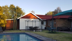 Um quintal com piscina, móveis de jardim e área coberta para sentar.