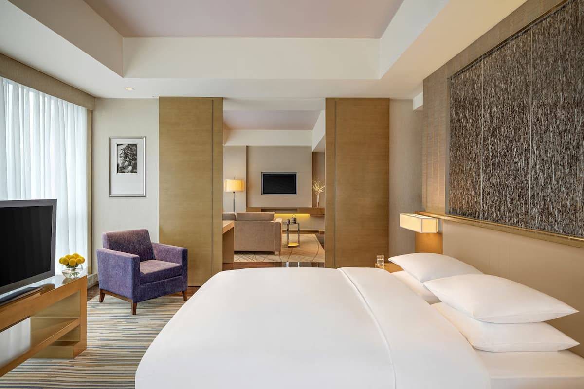 Quarto de hotel com uma cama grande, televisão, cadeira, escrivaninha e televisão na parede.