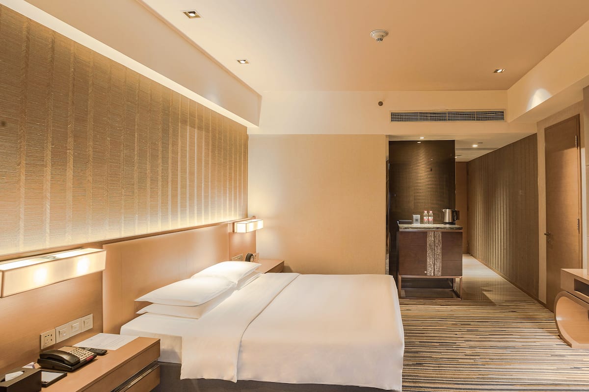 Quarto de hotel com uma cama grande, mesas de cabeceira, uma escrivaninha e um banheiro visível por uma porta aberta.