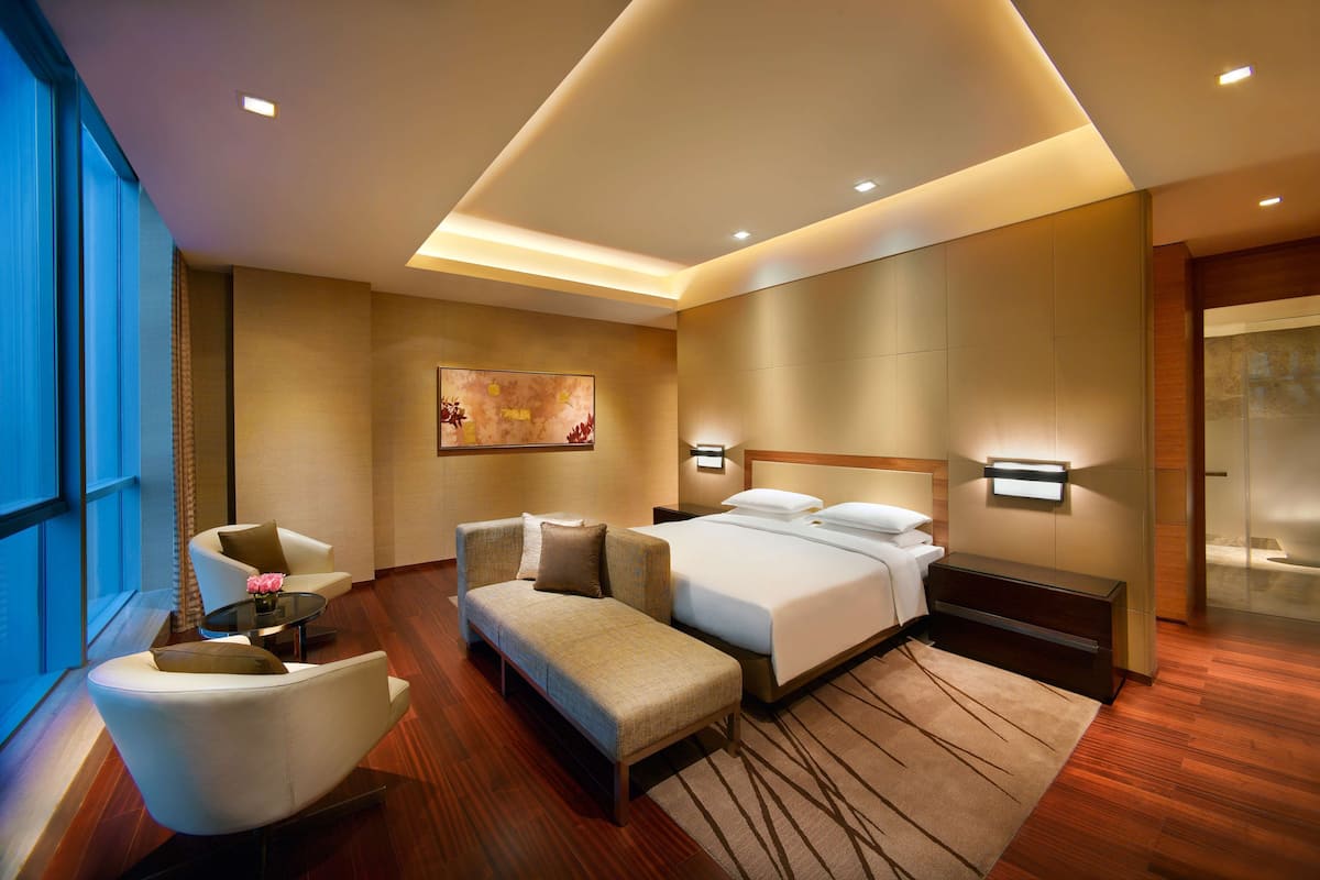Quarto de hotel moderno com uma cama grande, um sofá, uma mesa pequena e uma TV fixada na parede.