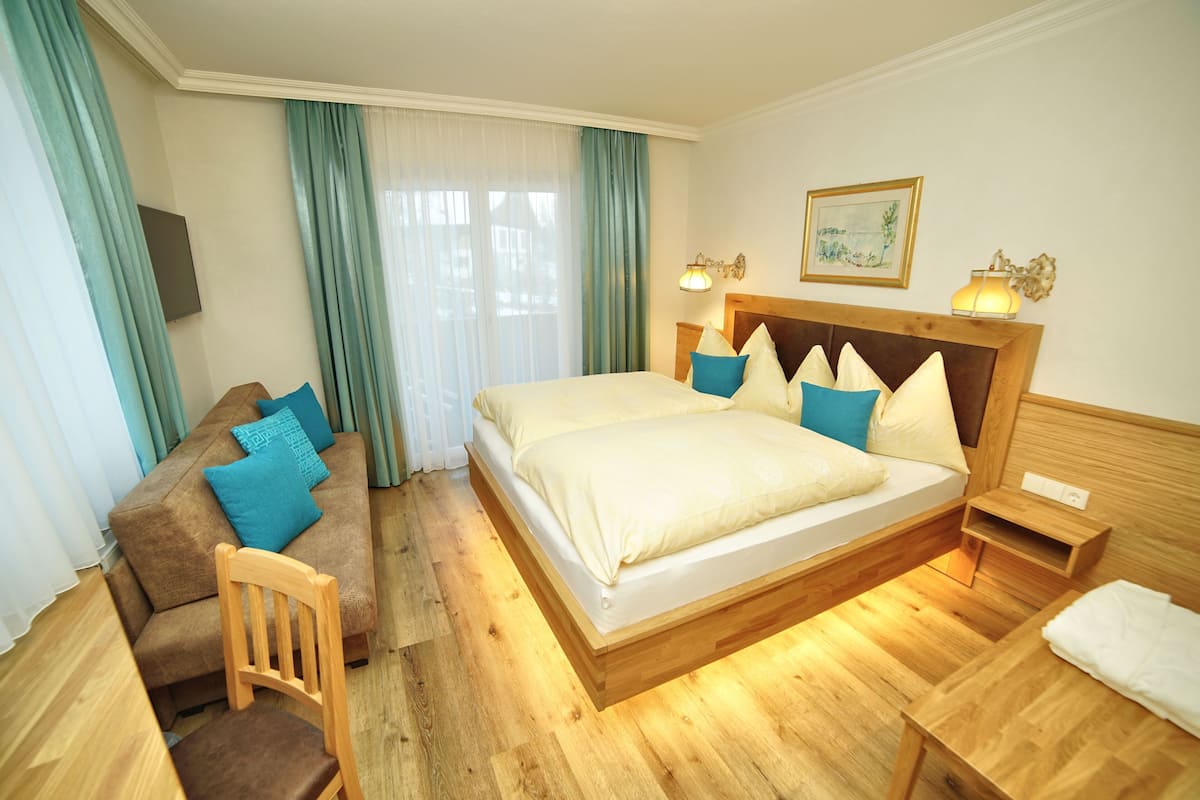 Quarto de hotel com cama, sofá, cadeira de madeira, mesa de cabeceira e abajur.