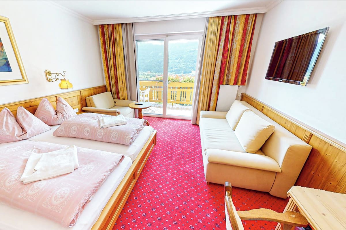 Quarto de hotel com uma cama grande, um sofá, uma mesa pequena e uma varanda com vista.