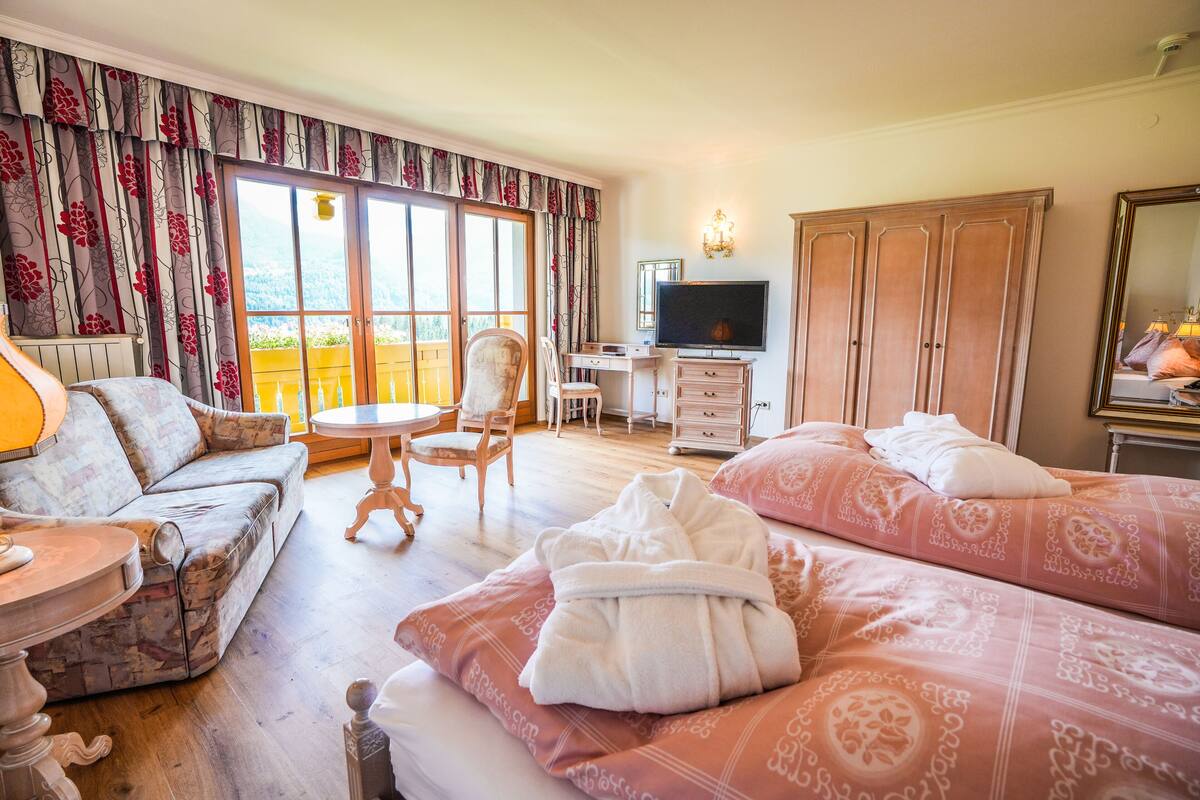 Quarto de hotel com sofá, duas camas com toalhas, escrivaninha com televisão, cadeira e guarda-roupa.