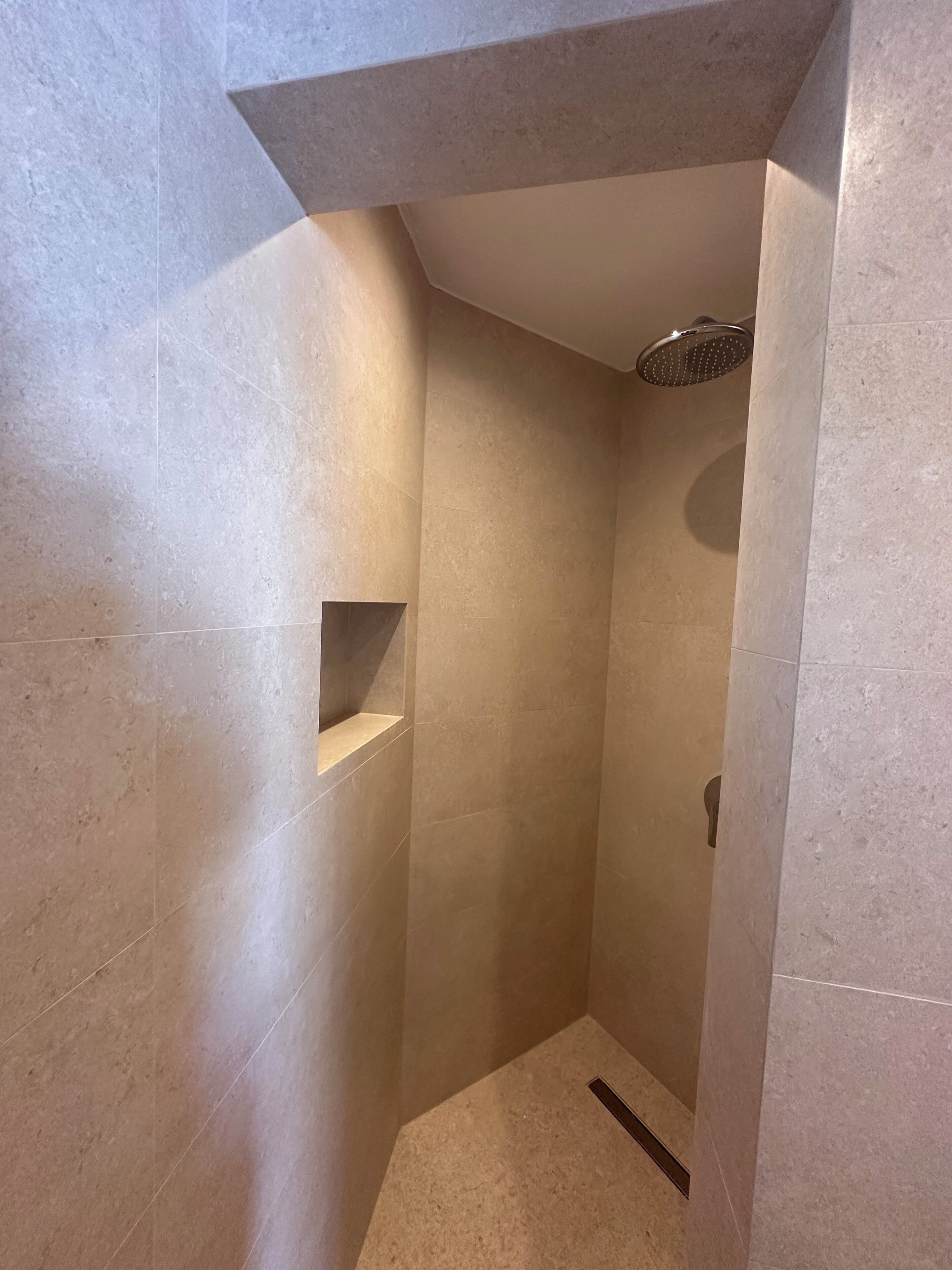 Pequeno espaço de duche com revestimento de azulejos, chuveiro e um prateleira.