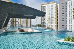 Um hotel moderno com uma grande piscina ao ar livre, edifícios altos ao fundo e uma estrutura preta marcante em primeiro plano.
