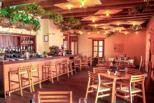 Restaurante com mobiliário de madeira, área de bar e plantas penduradas.