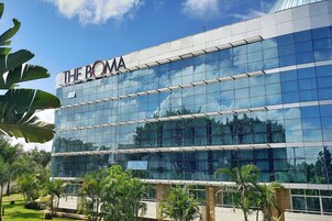 Um edifício moderno de vidro com a sinalização "THE BOMA", rodeado por vegetação.