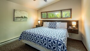 Quarto com cama, ventilador de teto, janela com vista para árvores e mesa de cabeceira com abajur.