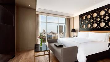 Quarto de hotel com uma cama grande, uma escrivaninha, uma cadeira, vista para a cidade e um painel decorativo na parede.