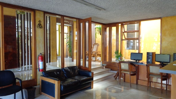 Ampla sala de estar com sofá de couro preto, móveis de madeira e escrivaninha com vários monitores.
