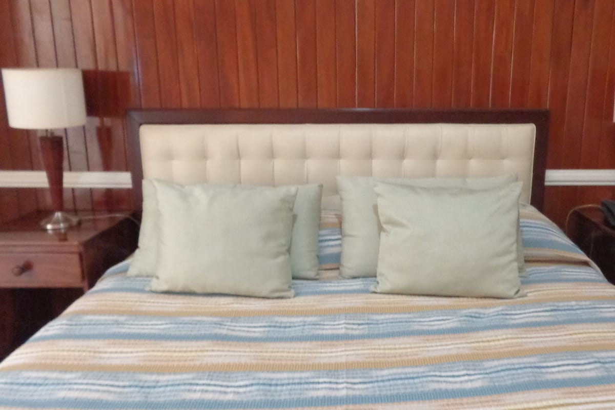 Uma cama com colcha listrada, duas almofadas e cabeceira de madeira.