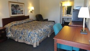 Quarto de hotel com cama, escrivaninha, cadeira, luminária, televisão e um quadro na parede.