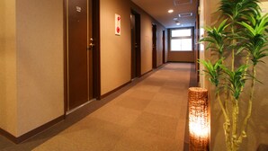 Um corredor de hotel com portas, uma placa e uma planta.