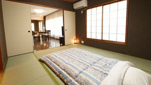 Um quarto japonês tradicional com tatames, futon, portas deslizantes e uma grande janela com biombos shoji.