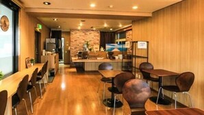 Um restaurante moderno com piso de madeira, cadeiras pretas e uma parede de tijolos ao fundo.