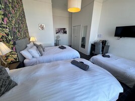 Quarto de hotel com duas camas, uma televisão, um espelho e papel de parede floral.