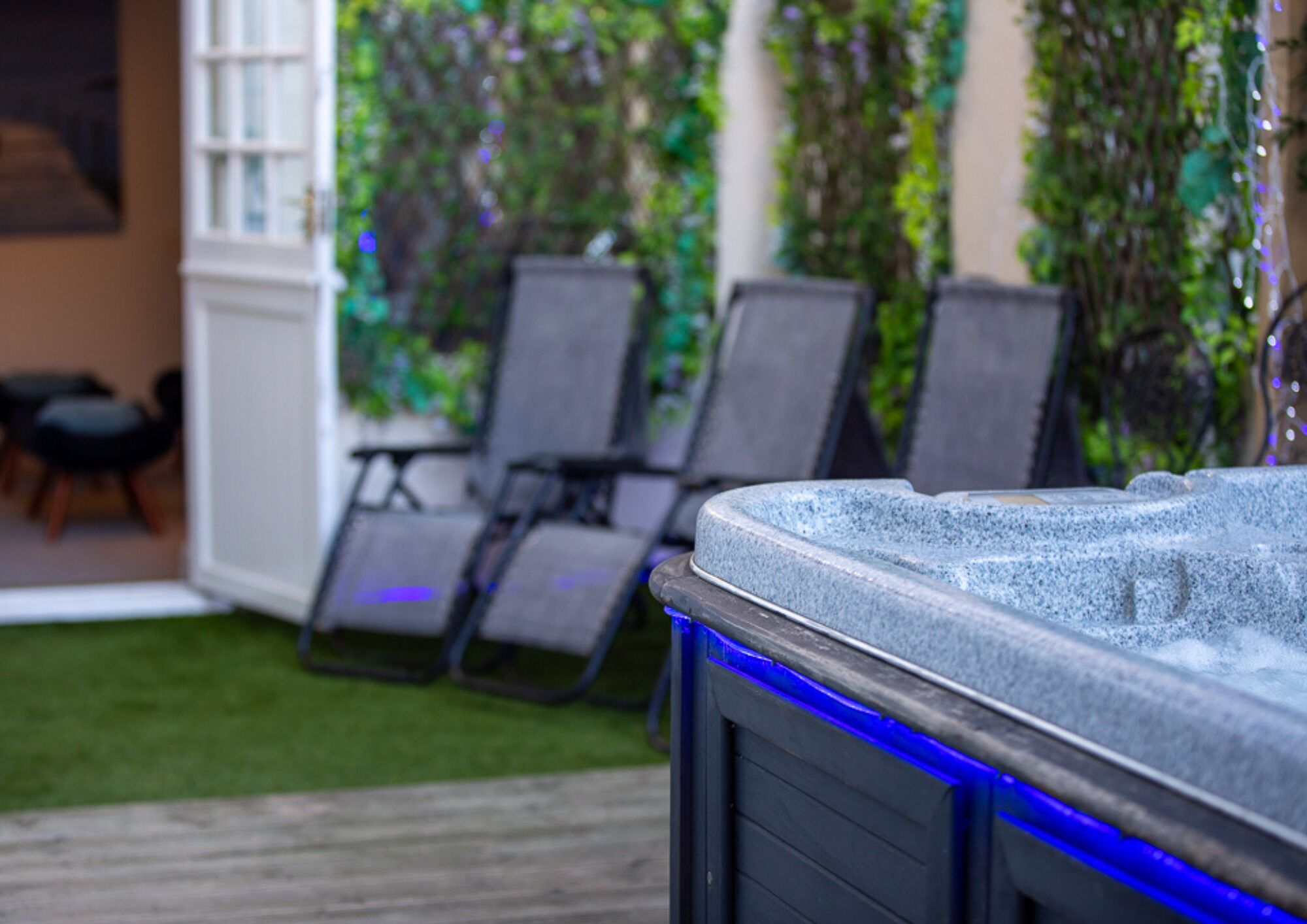 Uma banheira de hidromassagem com iluminação LED azul, rodeada por assentos externos com estrutura de metal e almofadas.