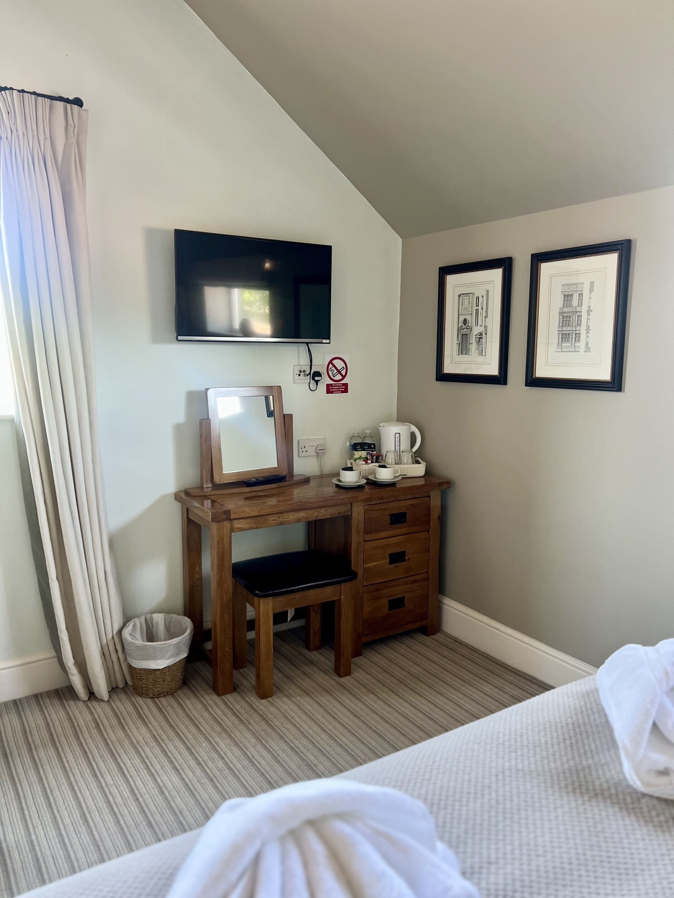 Quarto de hotel com escrivaninha de madeira, televisão de tela plana, obras de arte emolduradas, cama e janela com cortinas.