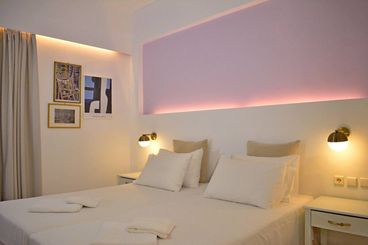 Quarto de hotel com cama bem arrumada, duas mesas de cabeceira e quadro pendurado na parede.