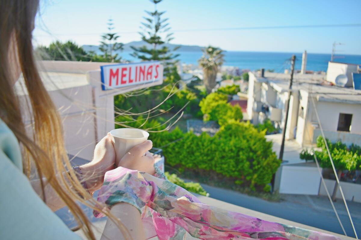 Vista da costa com uma placa indicando 'MELINAS' e uma pessoa segurando uma xícara.