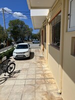 Rua residencial com um carro branco estacionado na lateral, uma bicicleta e um prédio com fachada bege.