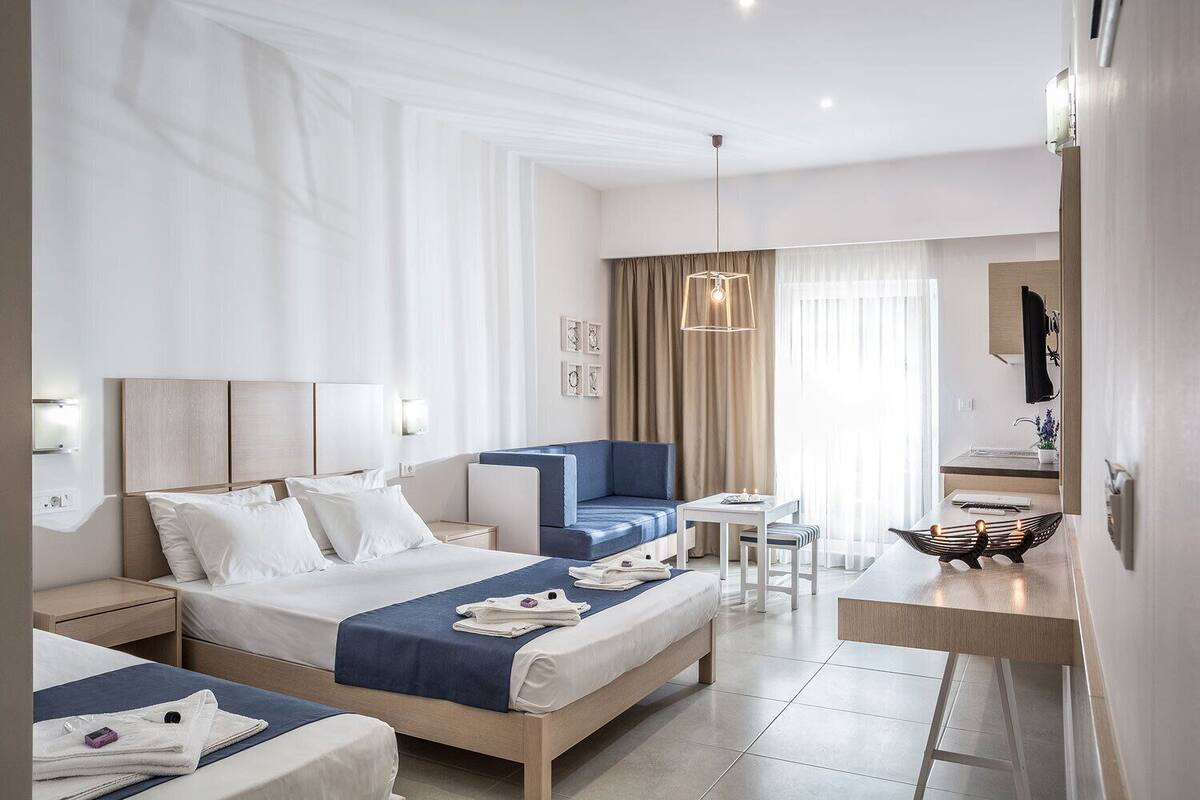 Quarto de hotel com cama, sofá, mesa pequena, cadeira, escrivaninha e espelho.