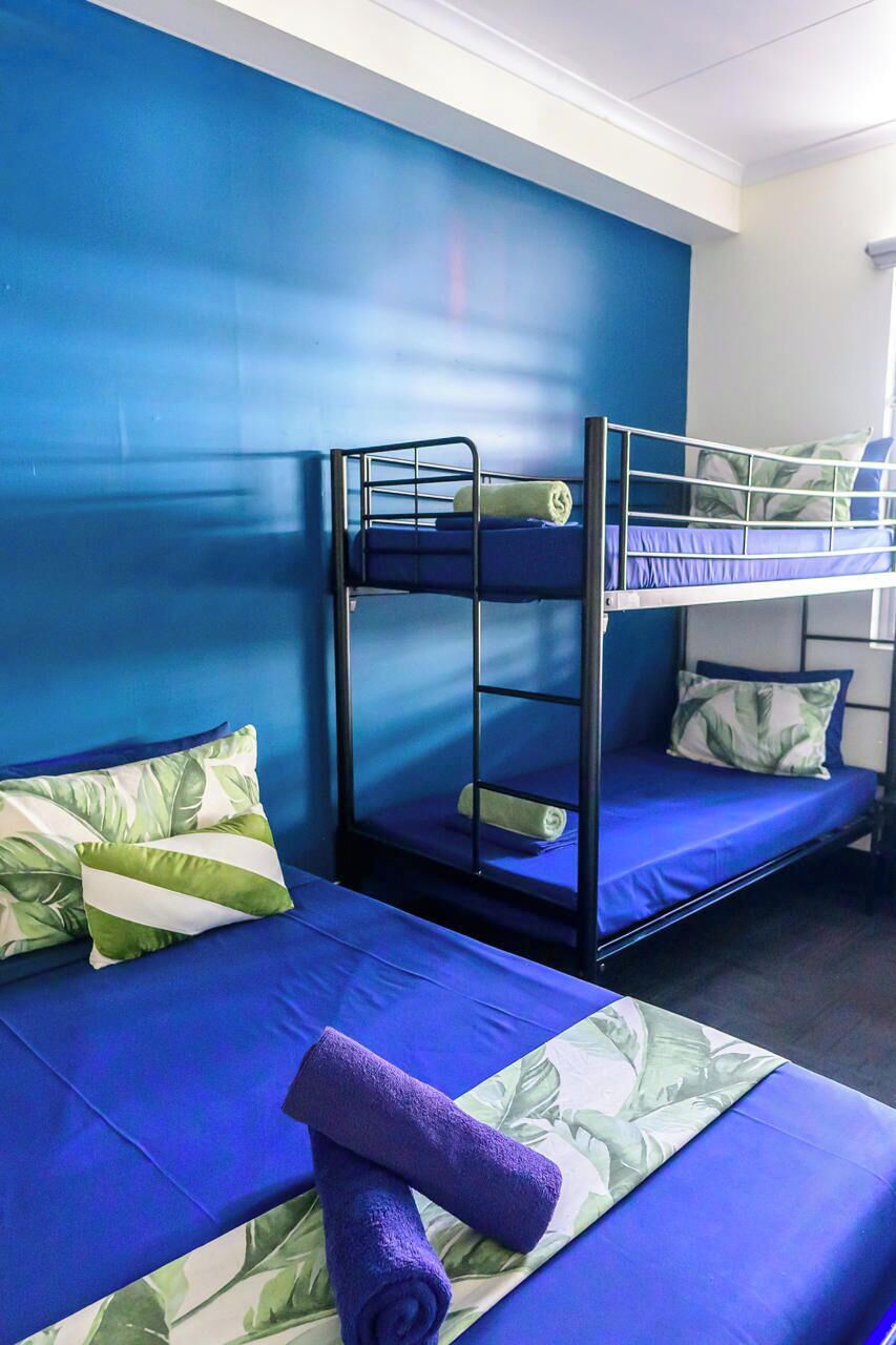 Quarto com beliche, roupa de cama e almofadas azuis, uma toalha enrolada no beliche inferior e uma janela ao fundo.